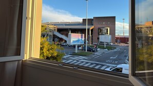 Visão pela janela de um prédio, com céu claro, rua com carros e uma placa.