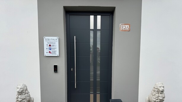 Uma fachada moderna com uma porta preta, uma placa com OTB Italia e duas estátuas de leão.
