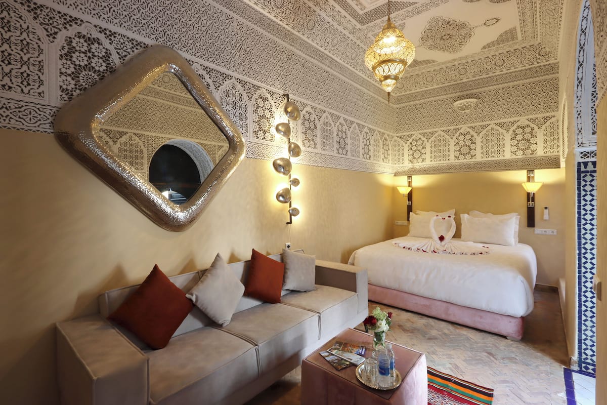 Quarto de hotel com sofá, cama, espelho e lustre.