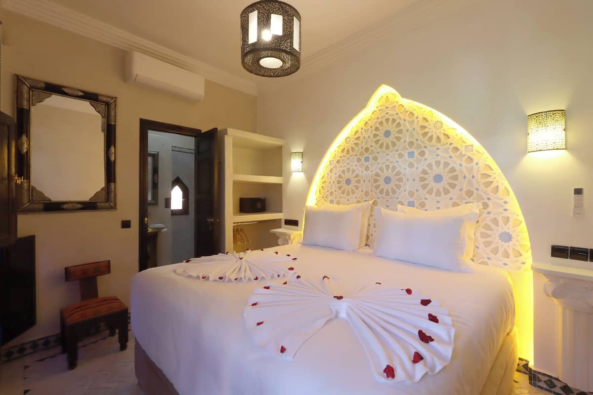 Quarto de hotel com cama, espelho, um banco e luminária na parede.