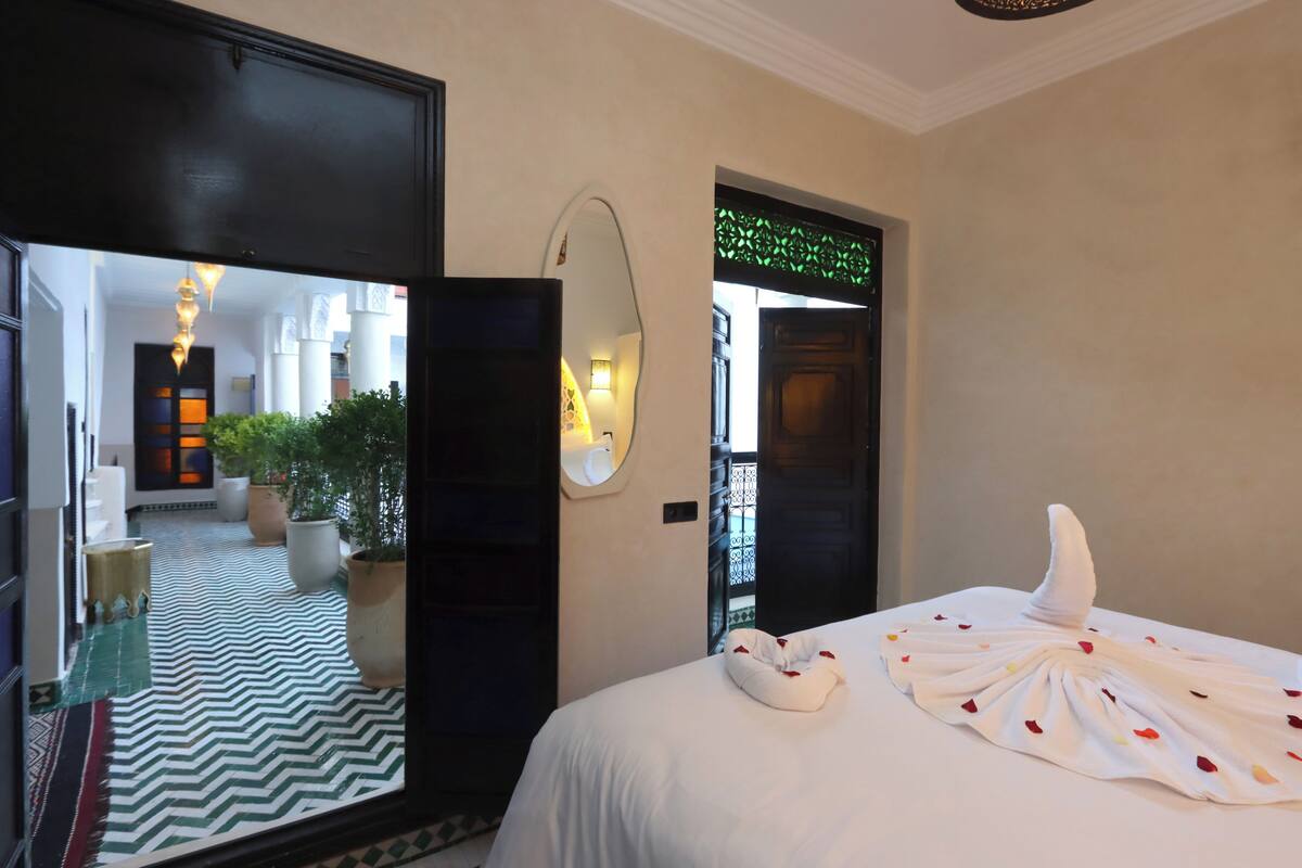 Quarto de hotel com cama, um espelho grande, uma planta em vaso e vista para o pátio.