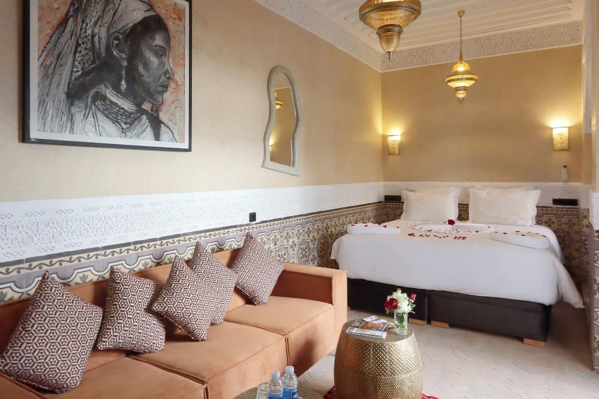 Quarto de hotel com cama, sofá, mesa de centro e espelho fixado na parede.