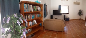 Uma sala de estar com estante de madeira, sofá bege, televisão e janela com cortinas.