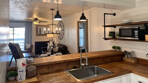 Cozinha moderna com bancada de madeira, pia de aço inoxidável e micro-ondas preto.