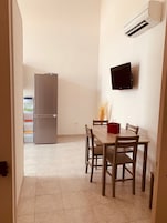 Uma cozinha compacta com geladeira embutida, mesa de jantar com cadeiras e TV na parede.