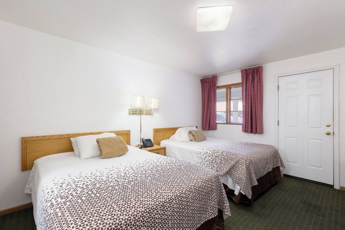 Quarto de hotel com duas camas, uma janela com cortinas, um abajur e uma porta.