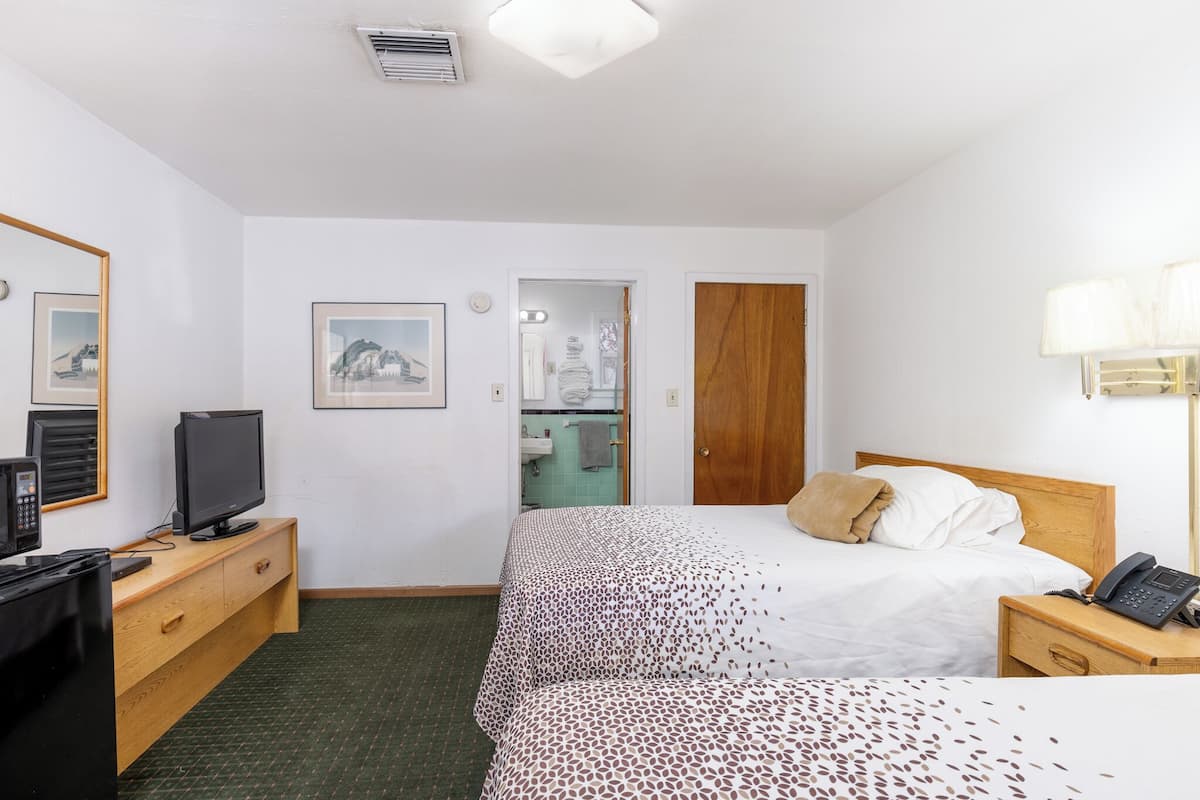 Quarto de hotel com cama, mesa de cabeceira, televisão, escrivaninha com computador e espelho.