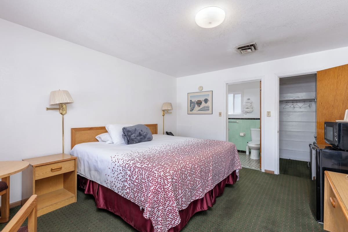Quarto de hotel com cama, mesas de cabeceira, escrivaninha, televisão e banheiro visível através de uma porta aberta.