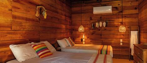 Quarto de cabana de madeira com duas camas, uma cômoda e um lustre.