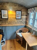 Quarto de canto com paredes de madeira, uma cadeira de vime, uma mesa de madeira e quadros nas paredes.