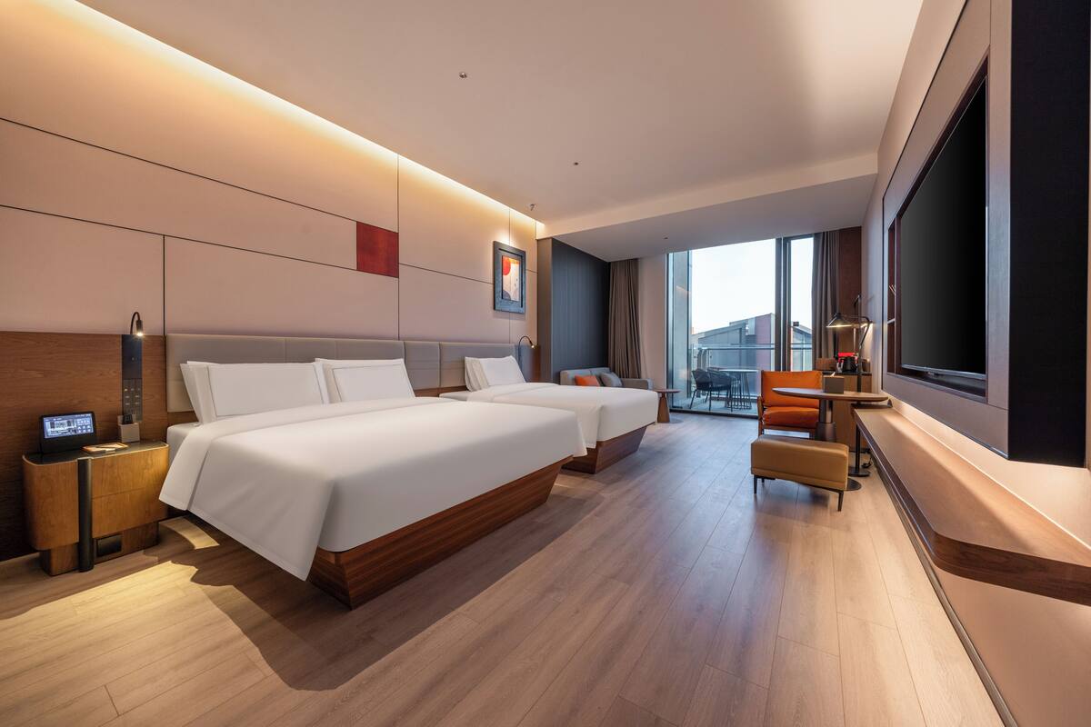 Quarto de hotel moderno com uma cama grande, uma escrivaninha e vista para a cidade.