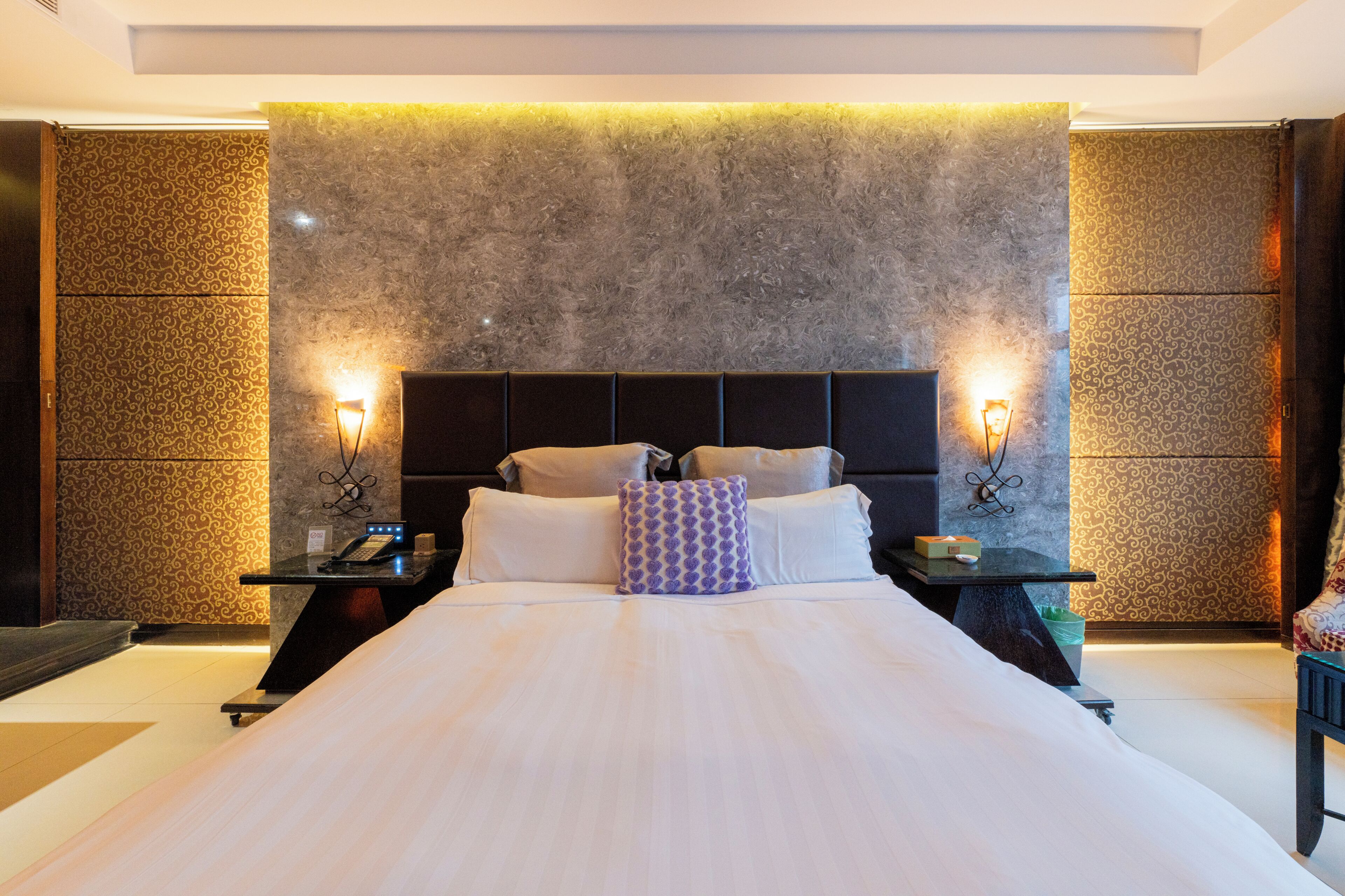 Quarto de hotel moderno com uma cama grande, duas mesas de cabeceira, uma cabeceira e uma parede texturizada.