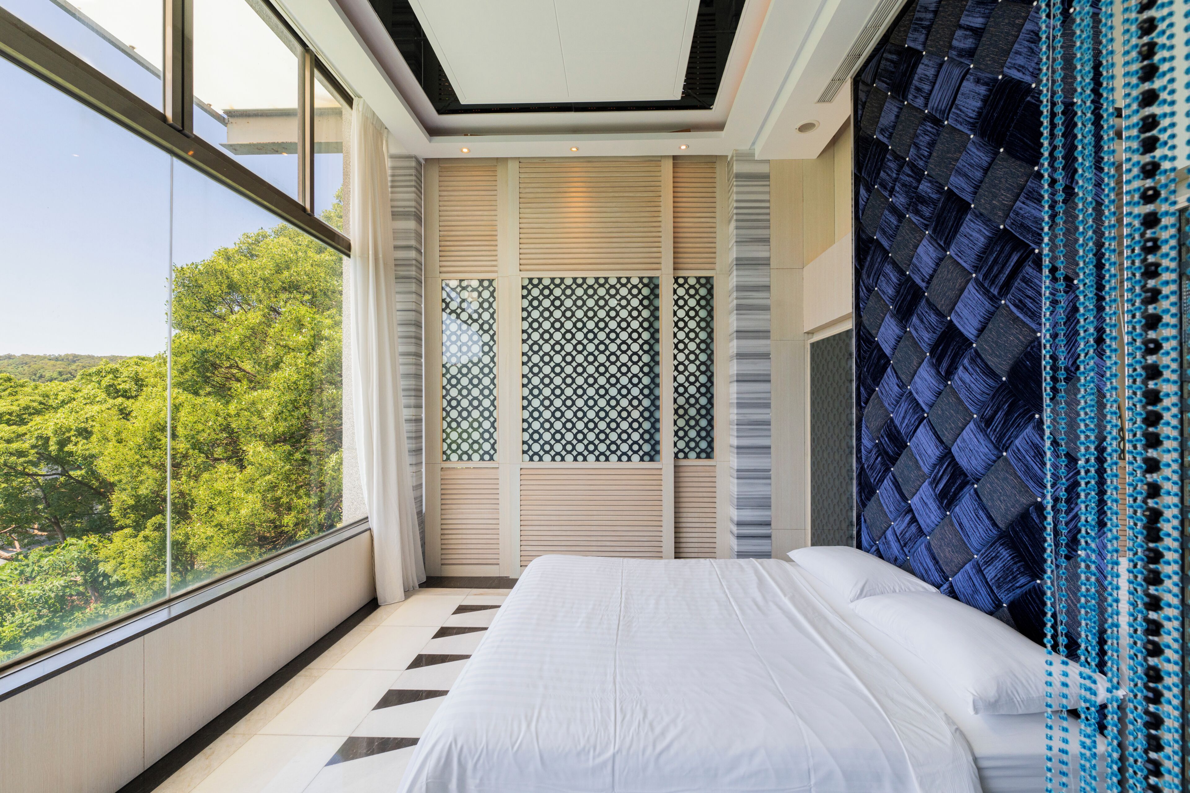 Quarto com uma janela grande, uma cama e vista para o verde lá fora.