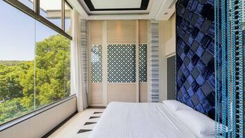 Quarto com uma janela grande, uma cama e vista para o verde lá fora.