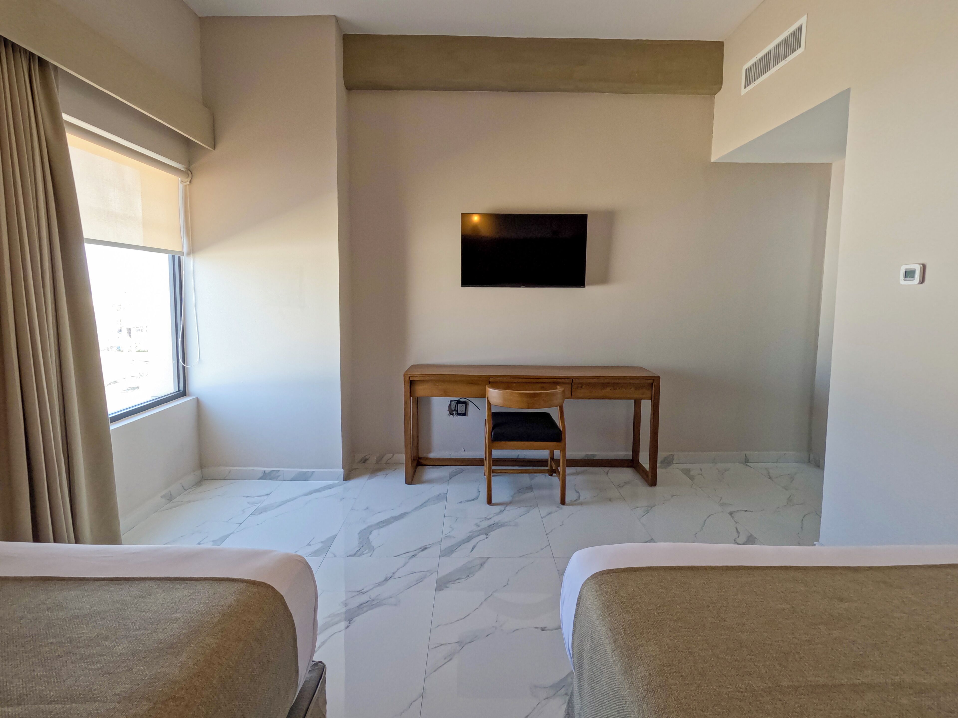Quarto de hotel com cama, secretária com cadeira, televisão na parede e janela com cortinas.