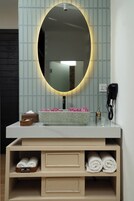 Casa de banho com espelho redondo, lavatório com cuba floral, secador de cabelo e estantes com toalhas.