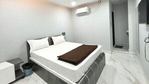 Quarto moderno com cama, ventilador de teto, aparelho de ar condicionado e uma pequena mesa de cabeceira.