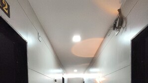 Um corredor com paredes brancas, piso de mármore e teto com iluminação embutida.