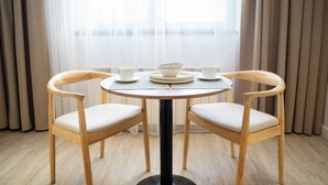 Mesa redonda com duas cadeiras, uma chávena branca, uma tigela e um prato sobre um apoio de mesa texturizado.