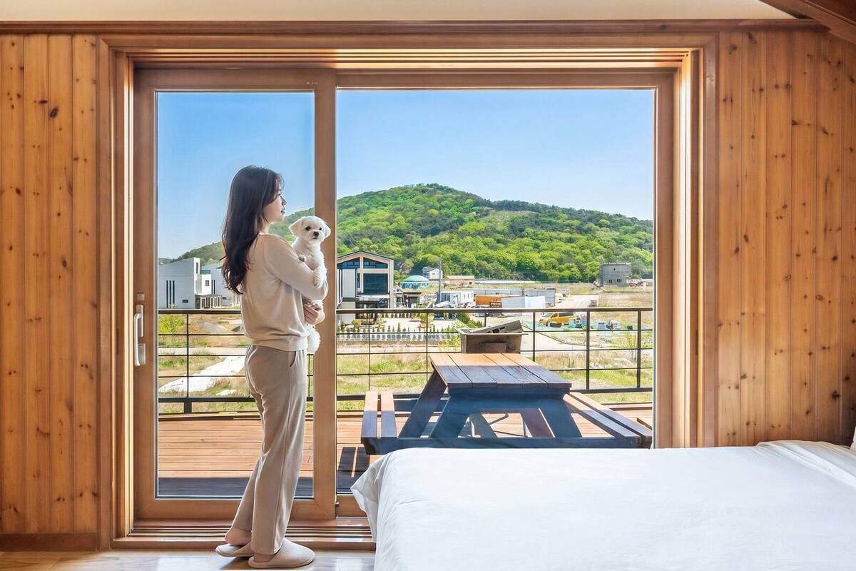 Quarto com uma grande porta de vidro deslizante, uma cama, um deck de madeira e vista para uma paisagem montanhosa.