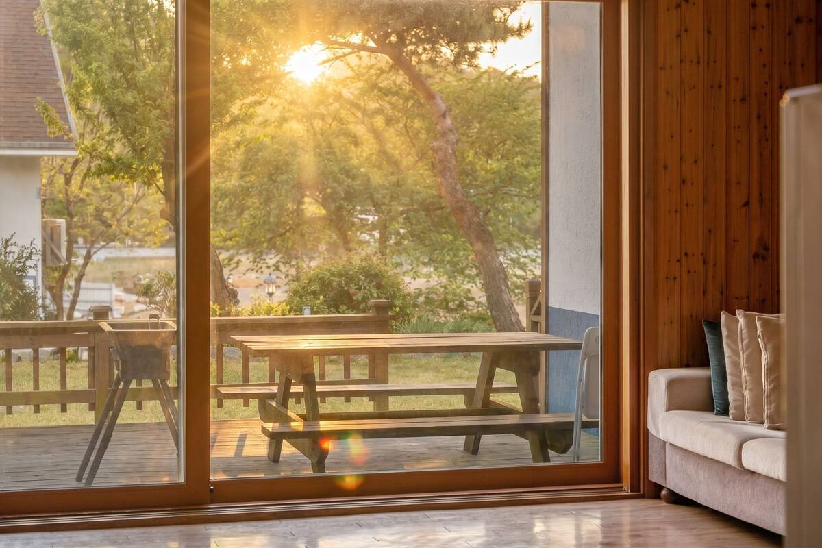 Quarto com porta de vidro deslizante que dá para um pátio externo com mesa e bancos de madeira.
