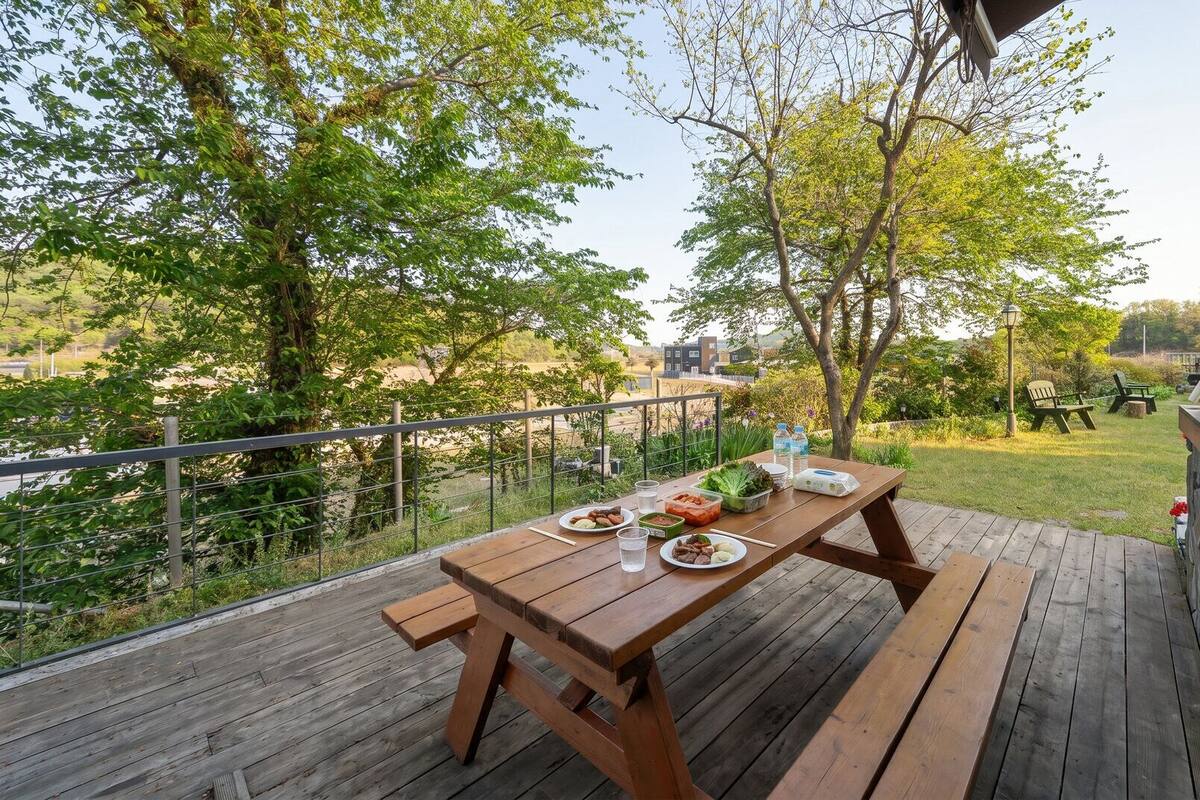 Um deck de madeira com uma mesa de piquenique, cercado por árvores e uma vista para a água.