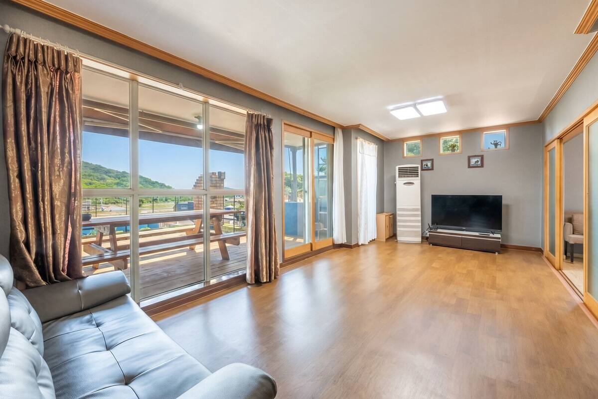 Uma sala de estar espaçosa com um sofá grande, uma televisão de tela plana e uma varanda com vista para a paisagem.