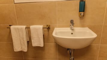 Um banheiro com pia branca, porta-toalhas com duas toalhas brancas e um dosador de sabonete azul.