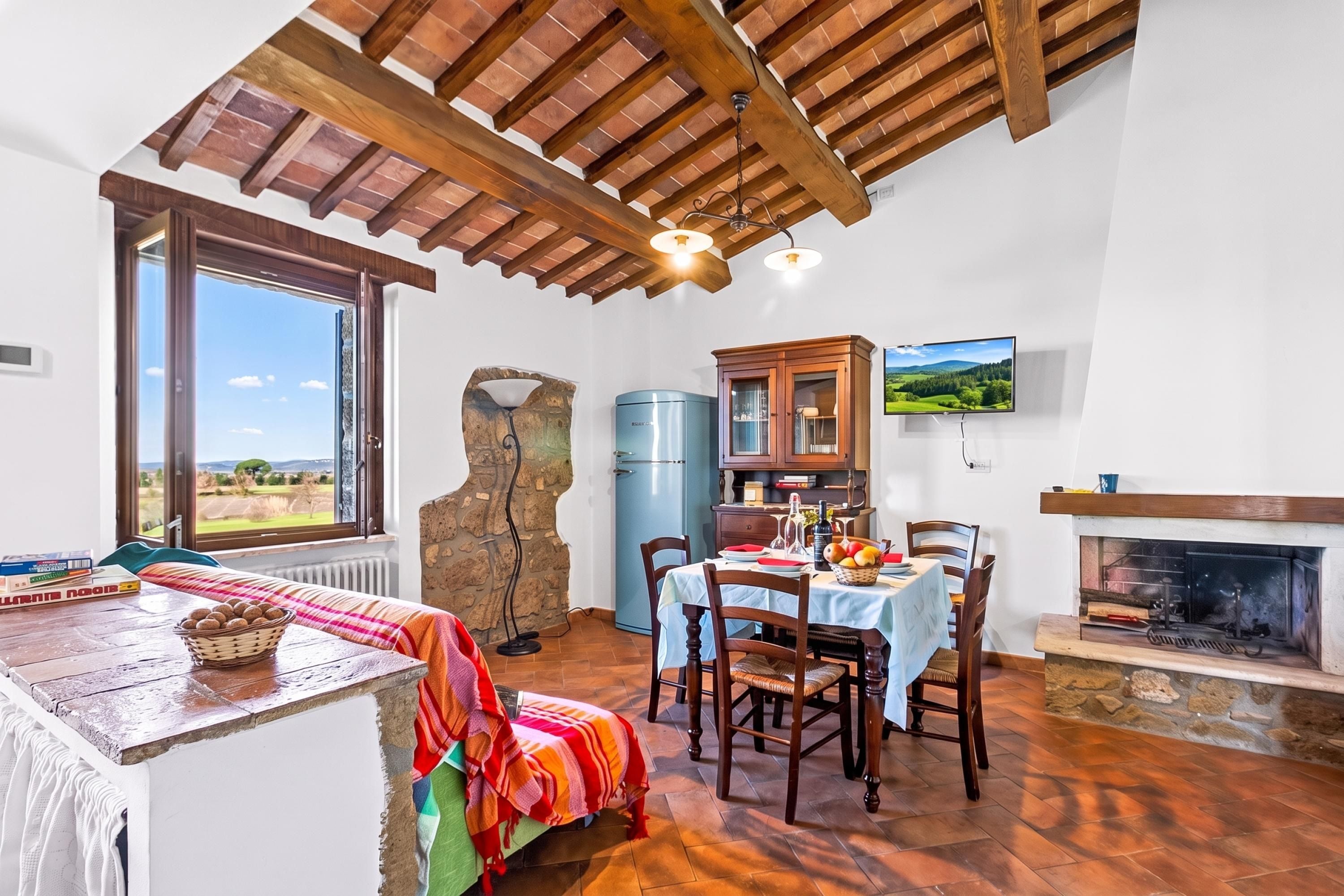 Cozinha rústica com parede de pedra, vigas de madeira no teto, mesa de jantar posta para quatro pessoas e lareira.