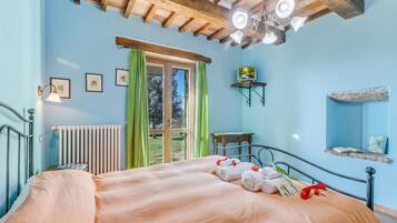 Quarto com cama, janela com cortinas, radiador, televisão e estante com livros.