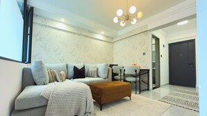 Uma sala de estar moderna com sofá, banqueta e poltronas, luminária no teto e uma porta.