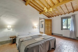 Quarto com cama, luminárias de cabeceira, porta de madeira e janela com cortinas.