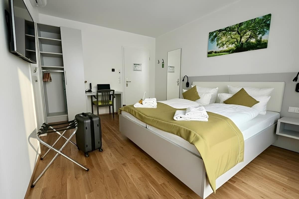 Quarto de hotel com uma cama, escrivaninha, cadeira, guarda-roupa e mala.