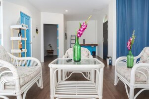 Uma sala de estar com móveis de vime, uma mesa de centro de vidro e dois vasos com flores.