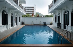 Piscina com exterior branco, rodeada por um muro branco e uma varanda com guardaílos pretos.