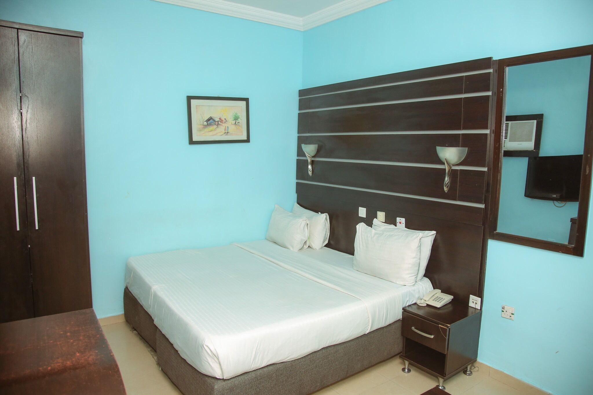 Quarto com cama, mesa de cabeceira, guarda-roupa e luminária na parede.