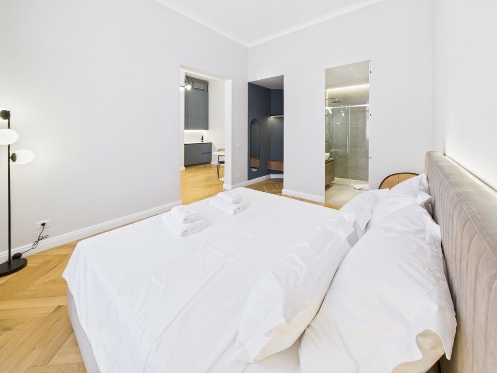 Quarto moderno com cama grande, mesa de cabeceira, abajur e closet espaçoso.