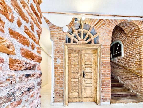 Um edifício rústico de tijolos com porta de madeira, parede de pedra e escadaria que leva a uma porta em arco.