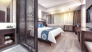 Quarto de hotel com cama, secretária, espelho, guarda-roupa e zona de casa de banho.