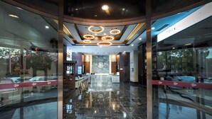 Um hall de hotel com piso de mármore, balcão de recepção e um lustre moderno.