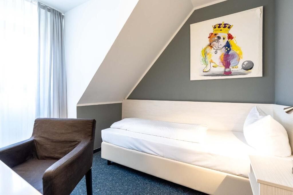 Quarto de hotel com uma cama, uma cadeira e um quadro na parede.