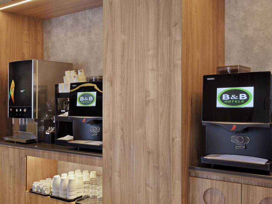 Uma estação de café com dosadores da marca e uma bandeja de copos descartáveis.