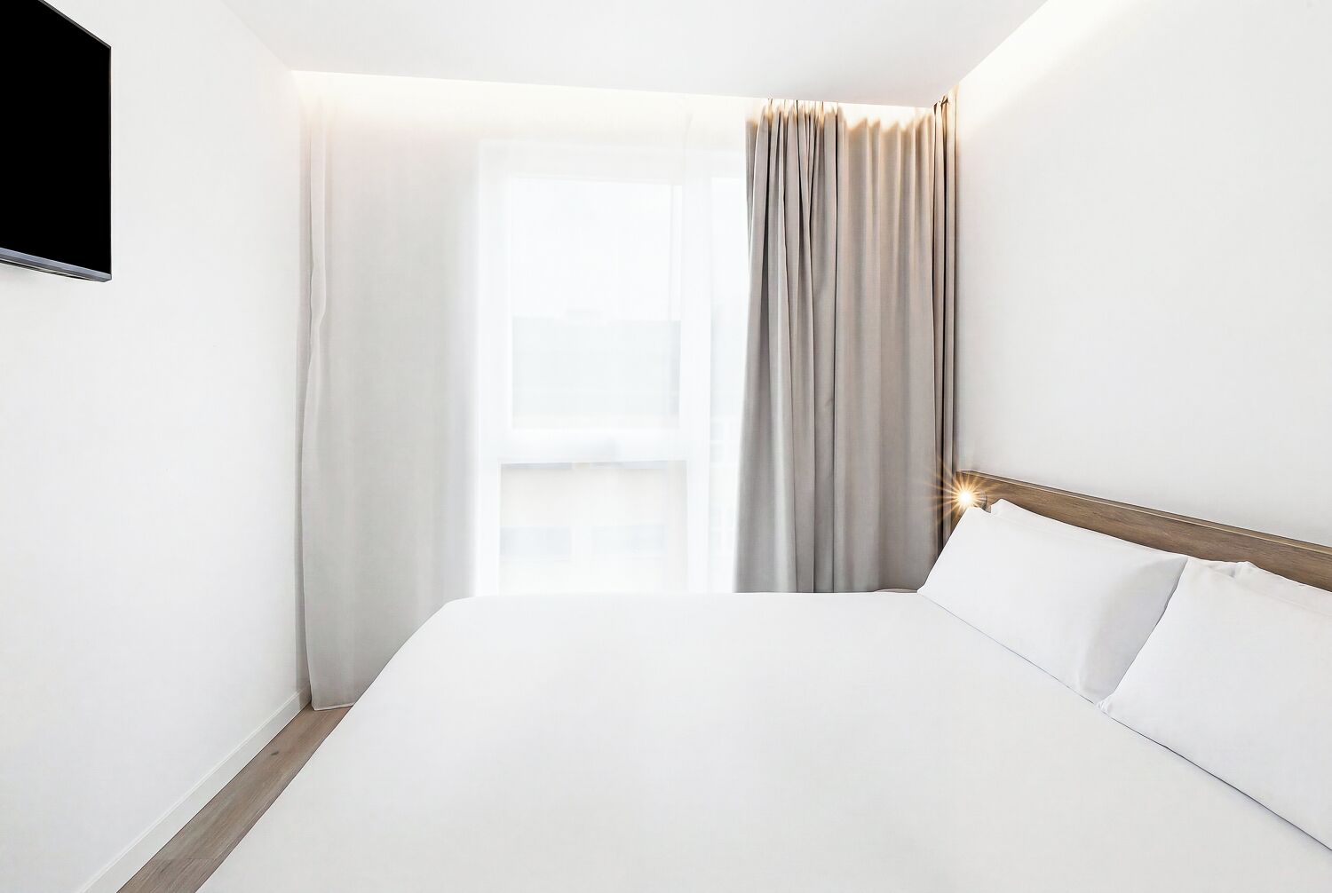 Quarto de hotel com uma cama, uma televisão na parede e uma janela com cortinas.