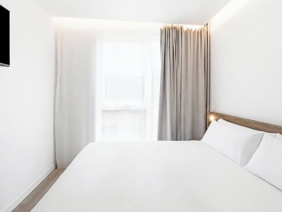Quarto de hotel com uma cama, uma televisão na parede e uma janela com cortinas.