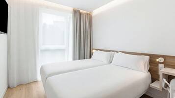 Quarto de hotel moderno com uma cama grande, uma mesa de cabeceira e uma janela com cortinas.