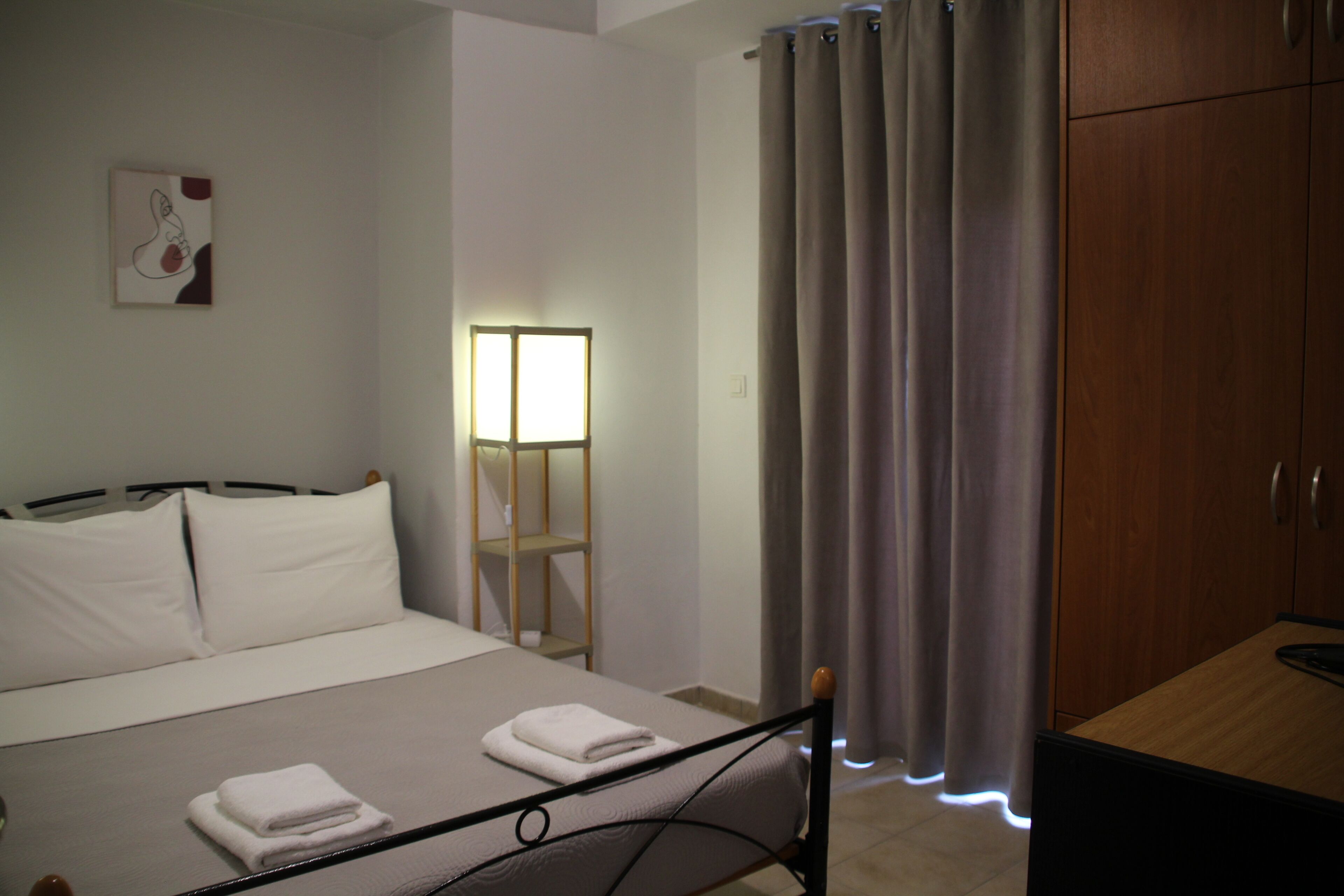 Quarto de hotel com cama, mesa de cabeceira, luminária, guarda-roupa e cortina.
