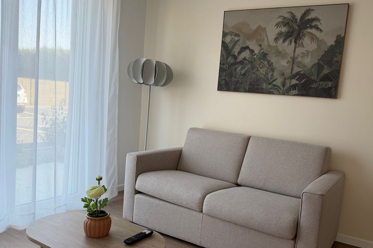 Sala de estar com sofá, mesa com planta, controle remoto e um quadro na parede.