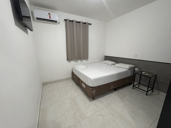 Quarto com cama, mesa de cabeceira, ar condicionado e cortina.