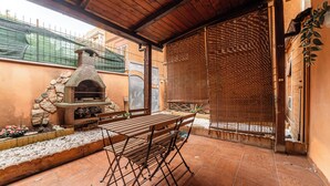 Um pátio ao ar livre com forno de pedra, mesa de madeira e cadeiras, e uma proteção.
