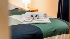 Quarto de hotel com cama, mesa de cabeceira, luminária e janela com cortinas.